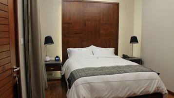 Cama bem arrumada com cabeceira de madeira, duas mesas de cabeceira com abajures e telefone ao lado da cama.
