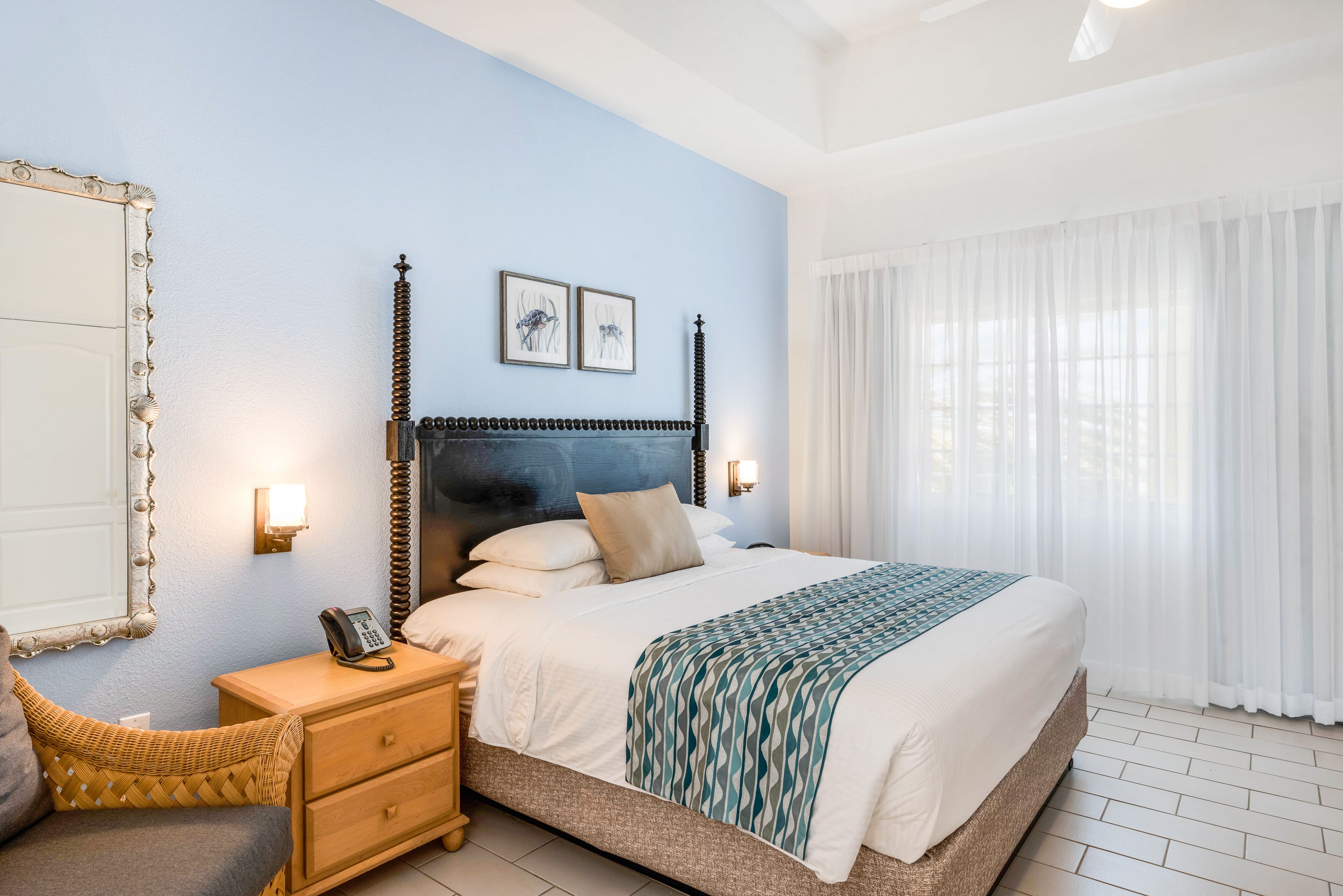 Quarto com uma cama grande, mesa de cabeceira com telefone, luz acoplada à parede e espelho.