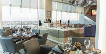Um lobby de hotel moderno com área de bar, espaço para refeições e vista da cidade.