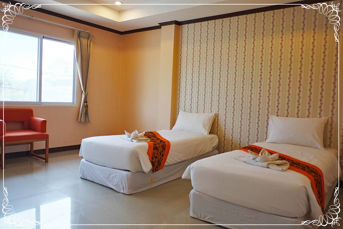 Quarto de hotel com duas camas, uma cadeira vermelha e uma janela com cortinas.