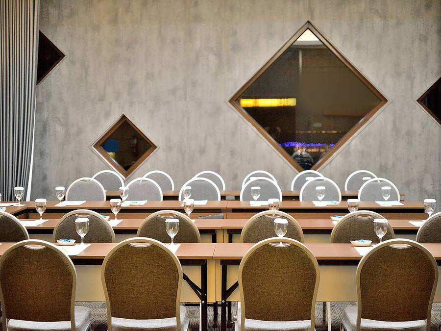 Sala de conferência com várias mesas e cadeiras, cada uma com um copo de água e um prato.