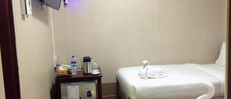 Quarto de hotel com uma cama, uma mesinha com chaleira, uma garrafa de água e um frigorífico.