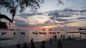 Uma praia ao pôr do sol com barcos e pessoas.