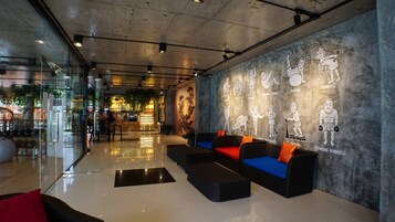 Um lobby moderno com parede de vidro, área de estar com sofás e parede com ilustrações sobre atividades físicas.