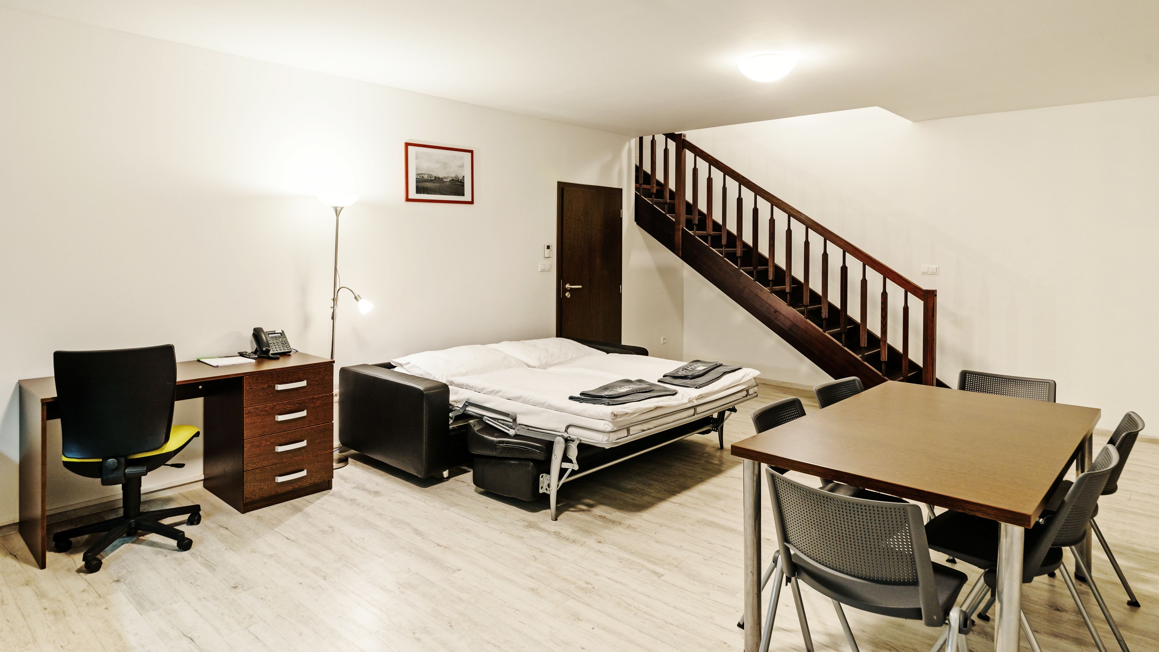 Quarto pequeno com cama, escrivaninha, cadeira e escada.