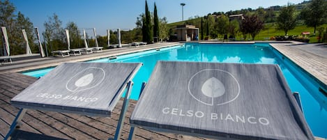 Uma piscina com espreguiçadeiras identificadas como "GELSO BIANCO" e um deck de madeira.