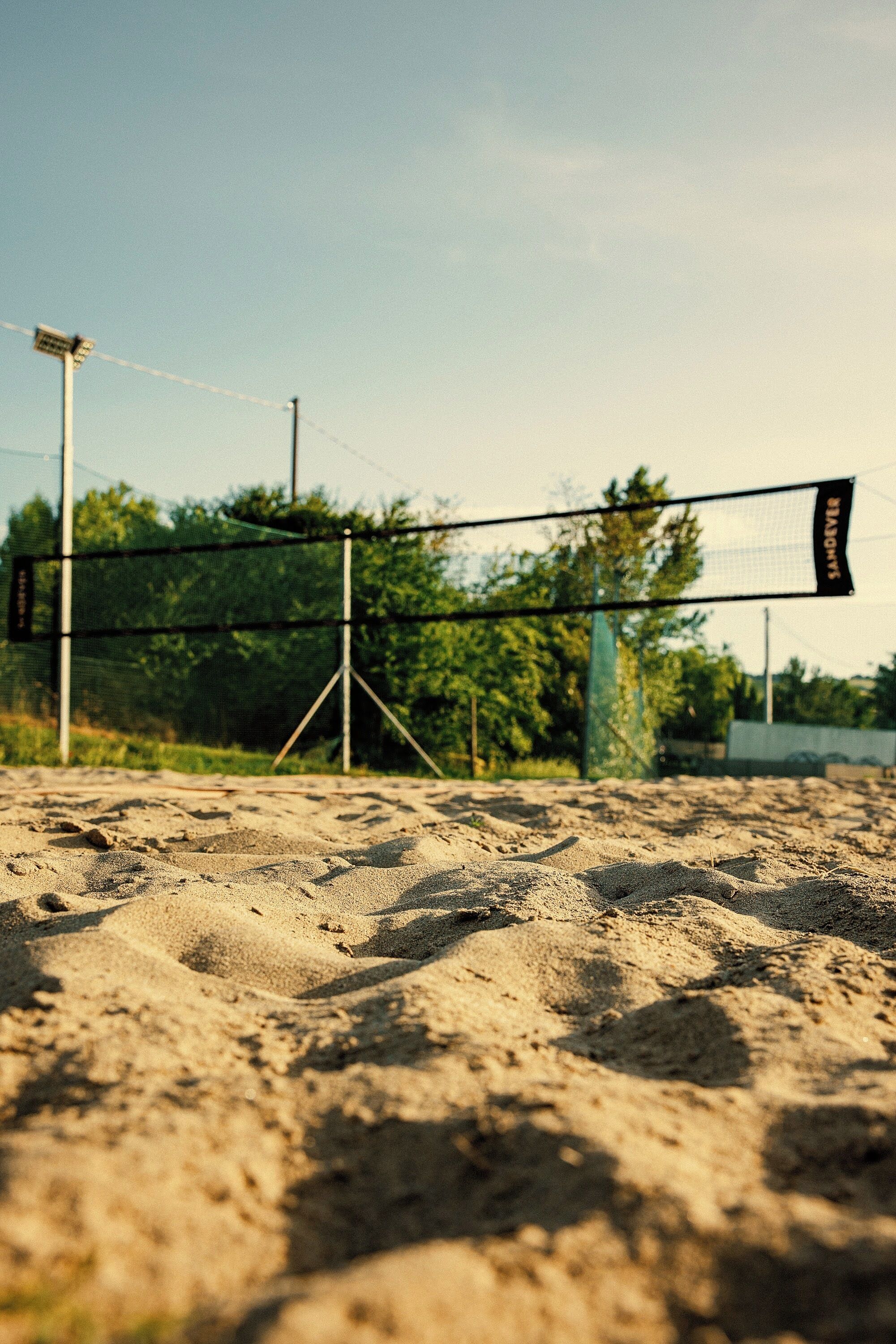 Uma quadra de voleibol de praia com areia, com uma rede identificada como 'Sandee'.