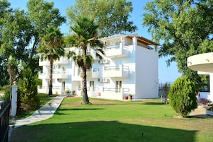 Um edifício moderno de vários andares com varandas, cercado por vegetação exuberante e palmeiras.