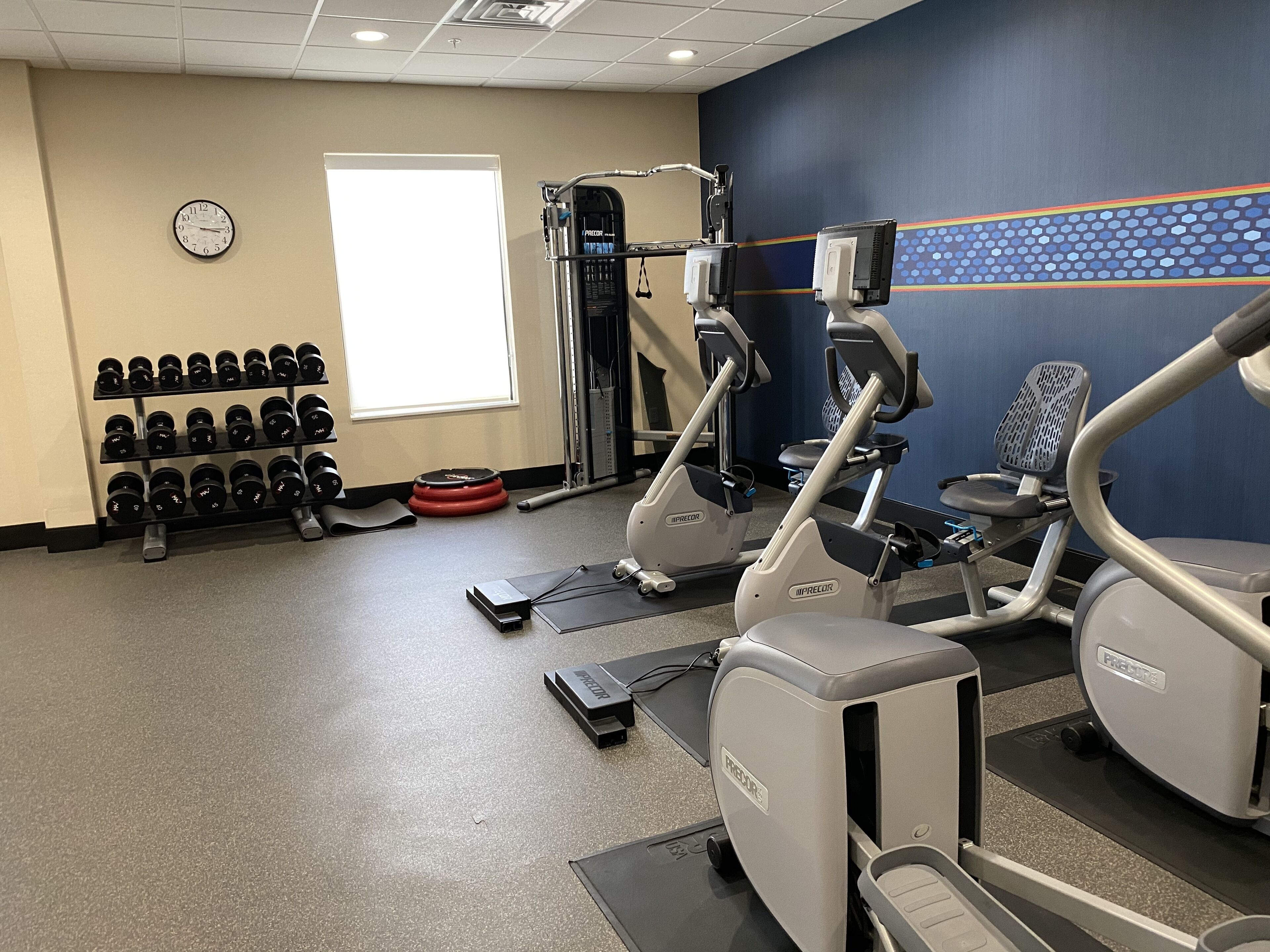 Uma academia com equipamentos de exercício, halteres e um relógio na parede.