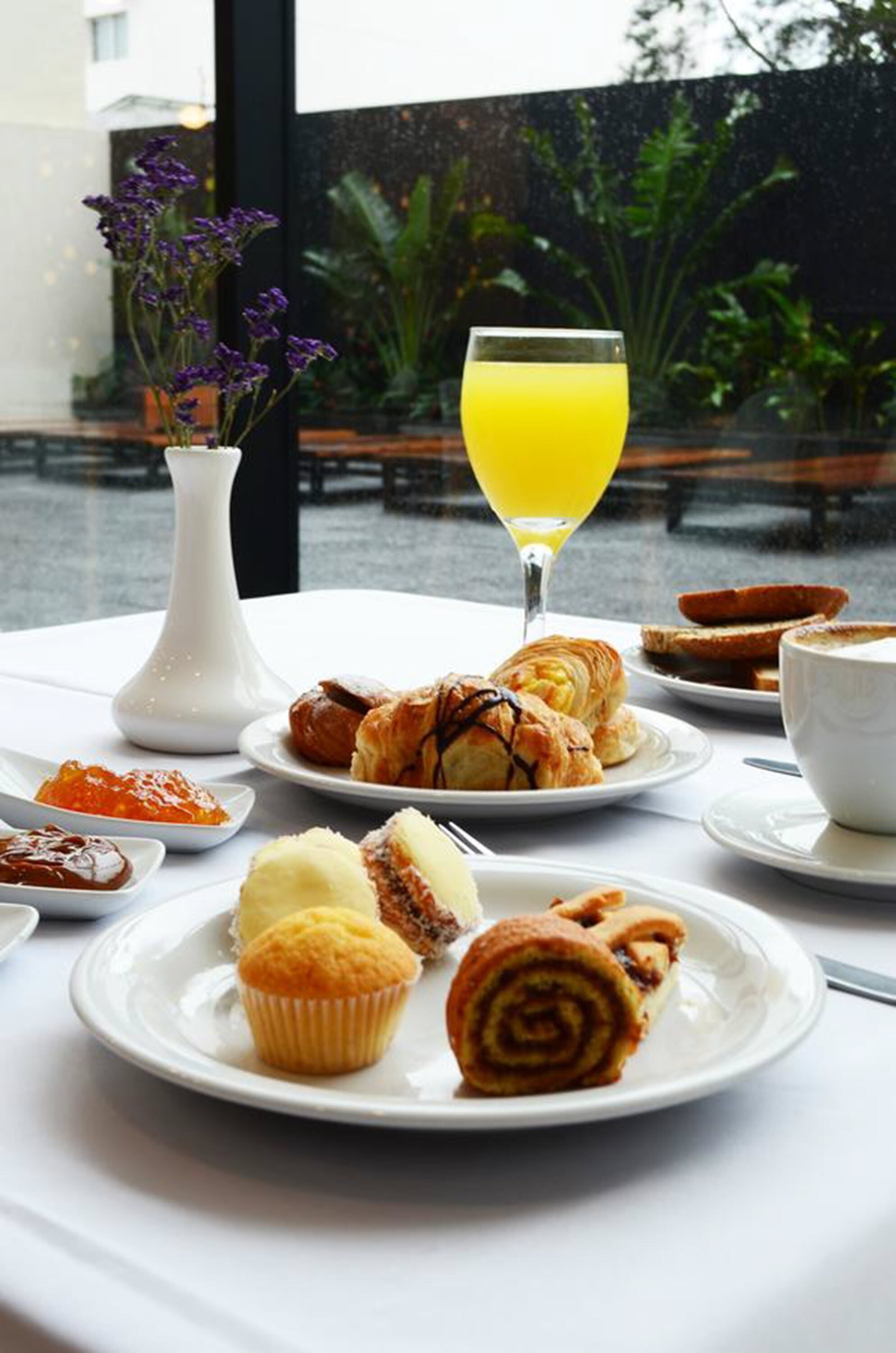 Uma mesa posta com doces, um copo de suco de laranja e um vaso de flores.
