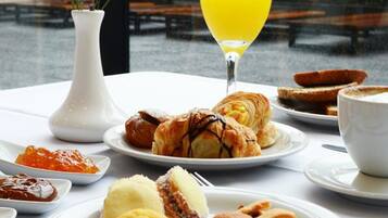 Uma mesa posta com doces, um copo de suco de laranja e um vaso de flores.