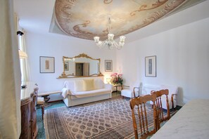 Um quarto amplo com um espelho grande, um sofá branco, uma cadeira de madeira e um tapete estampado.