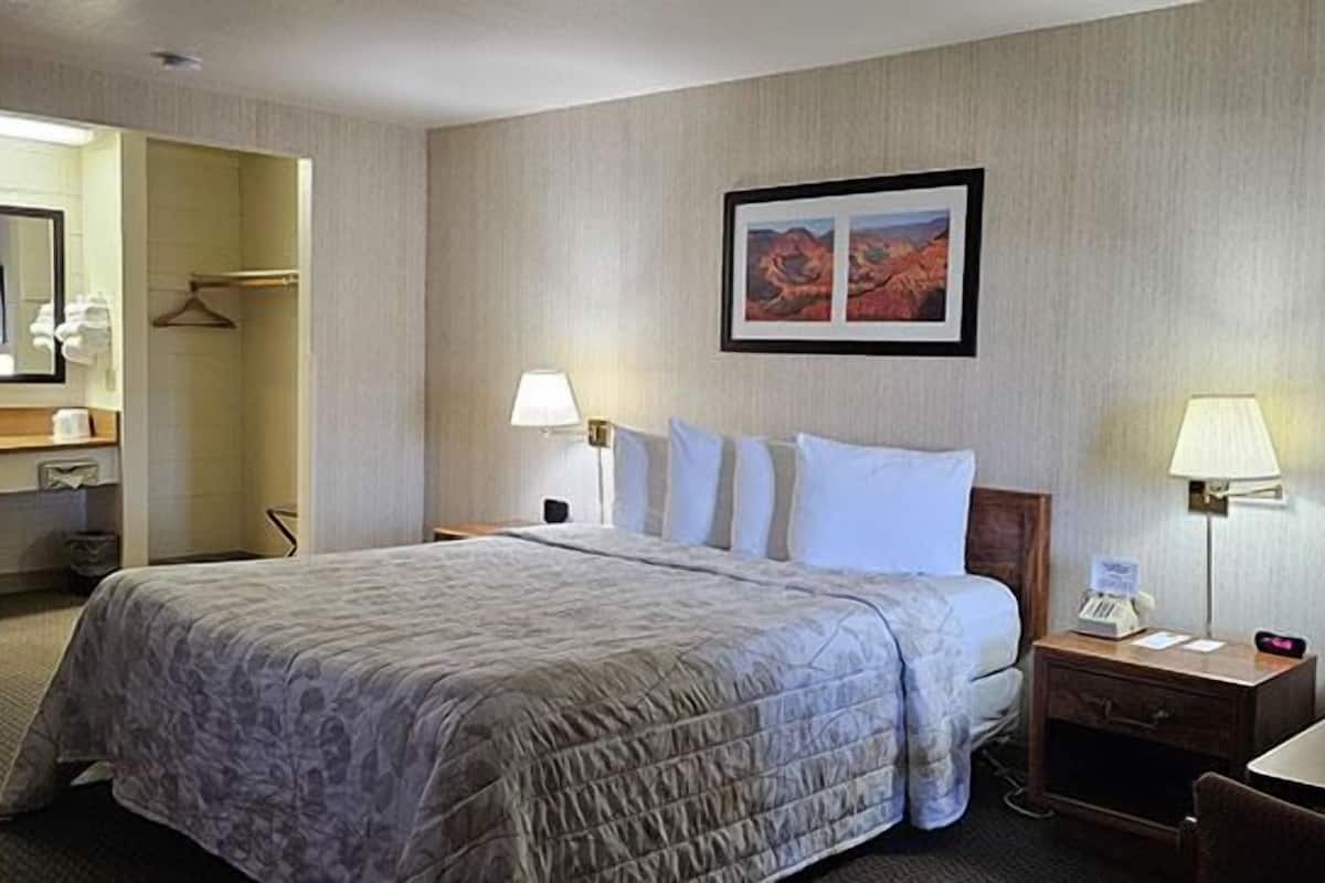 Quarto de hotel com cama, mesas de cabeceira, escrivaninha, cadeira, espelho e quadro na parede.
