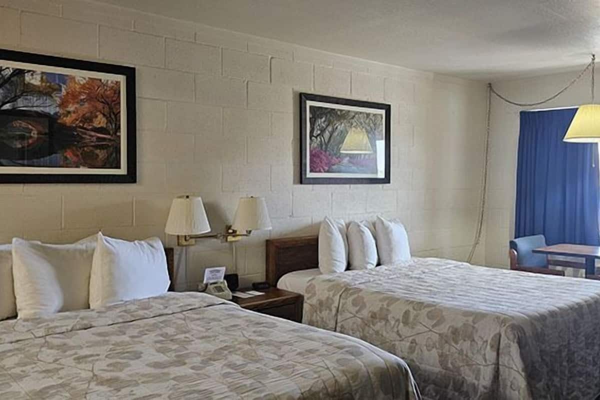 Quarto de hotel com duas camas, uma escrivaninha, uma cadeira e duas pinturas na parede.