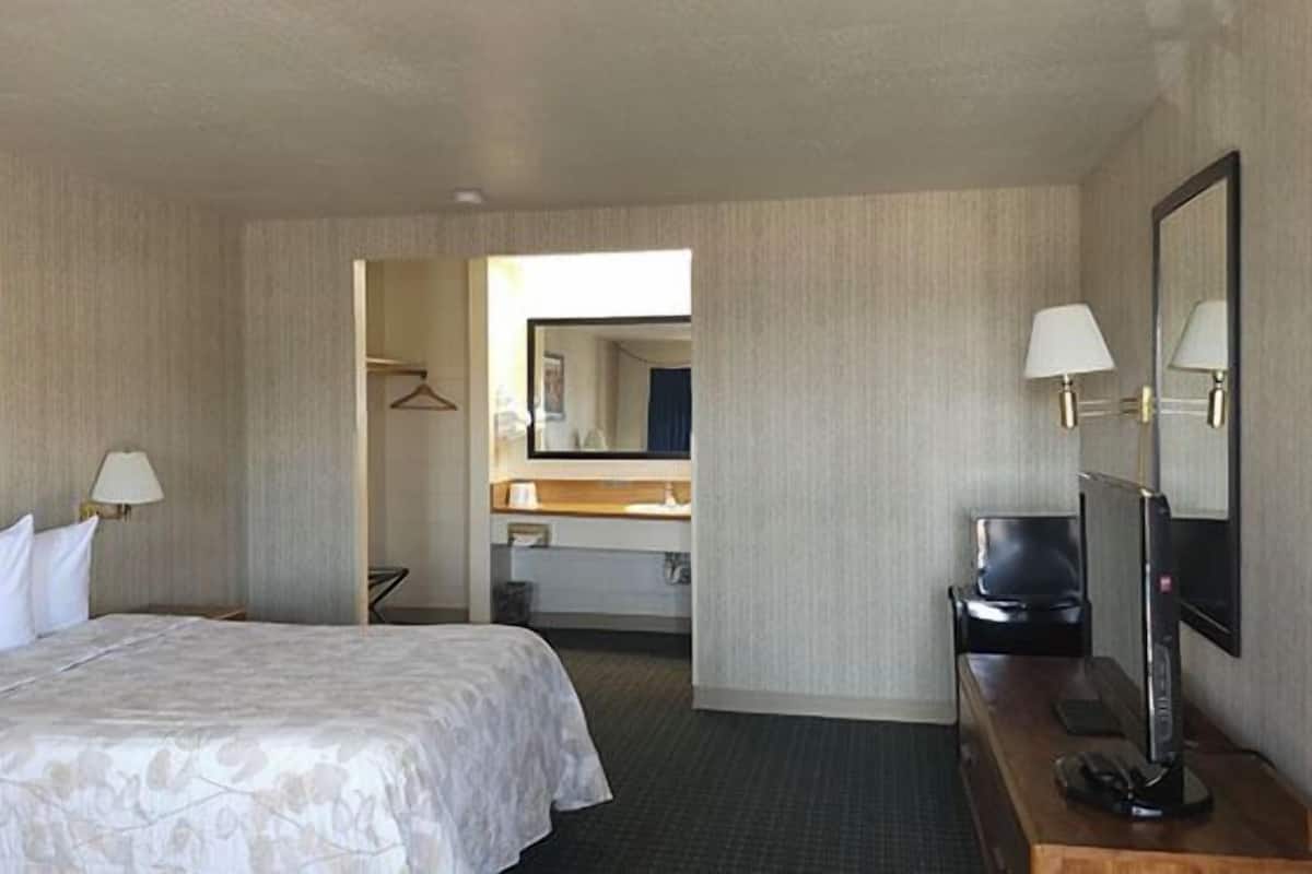 Quarto de hotel com cama, escrivaninha com computador, espelho e quadro na parede.