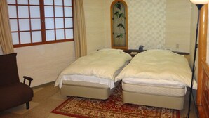 Quarto de hotel com duas camas, uma janela grande com cortinas, um espelho decorativo, uma mesa de cabeceira e um abajur.