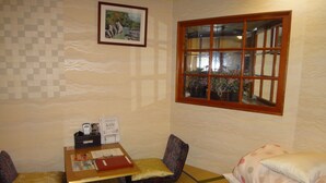 Quarto com parede xadrez, um quadro emoldurado, janela de madeira, mesa com pasta vermelha, duas cadeiras e um sofá estampado com bolinhas.