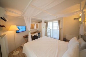 Quarto de hotel com uma cama grande, uma mesa de escritório com computador, televisão e janela com cortinas.