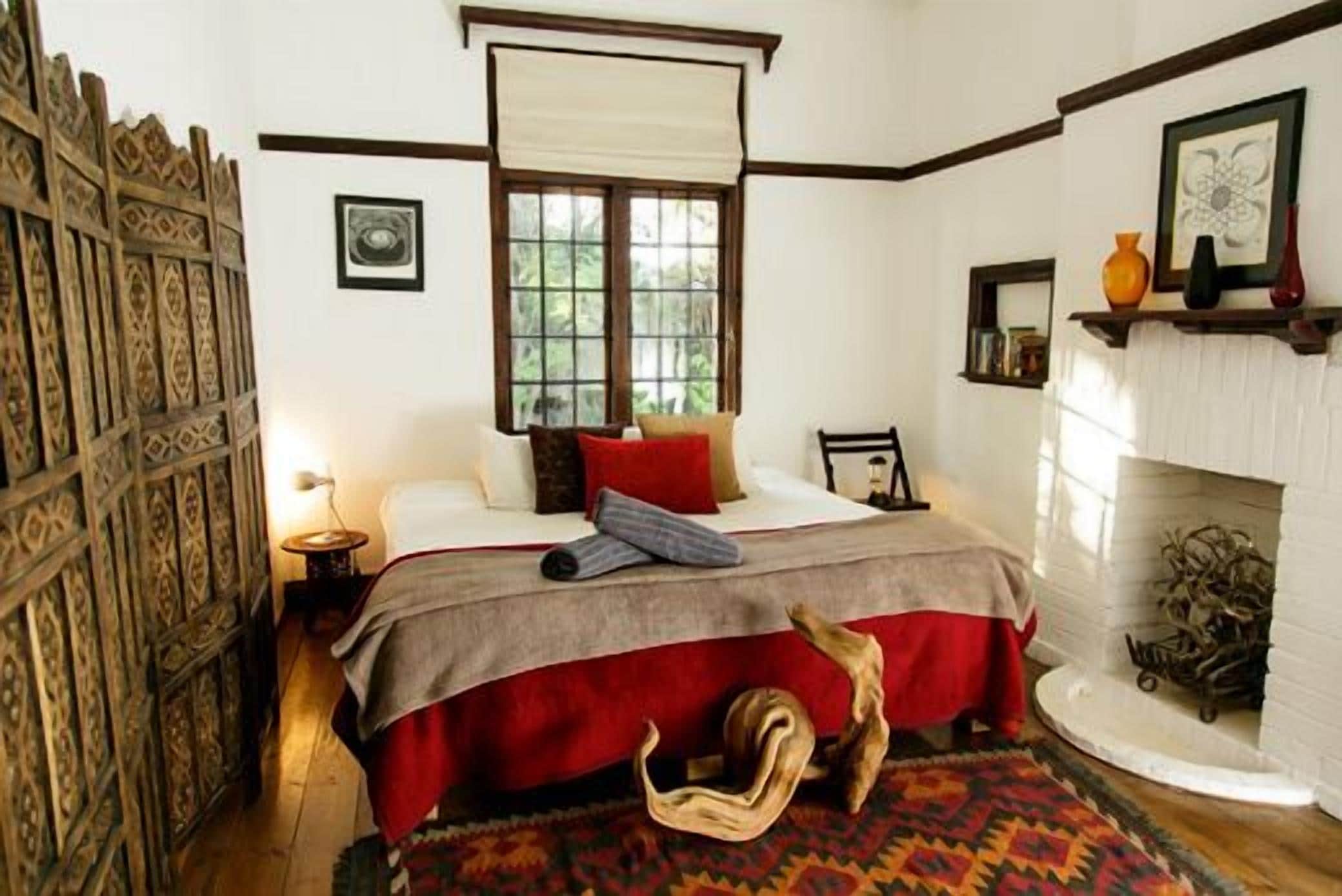 Quarto com cama, lareira, janela e painel decorativo na parede.