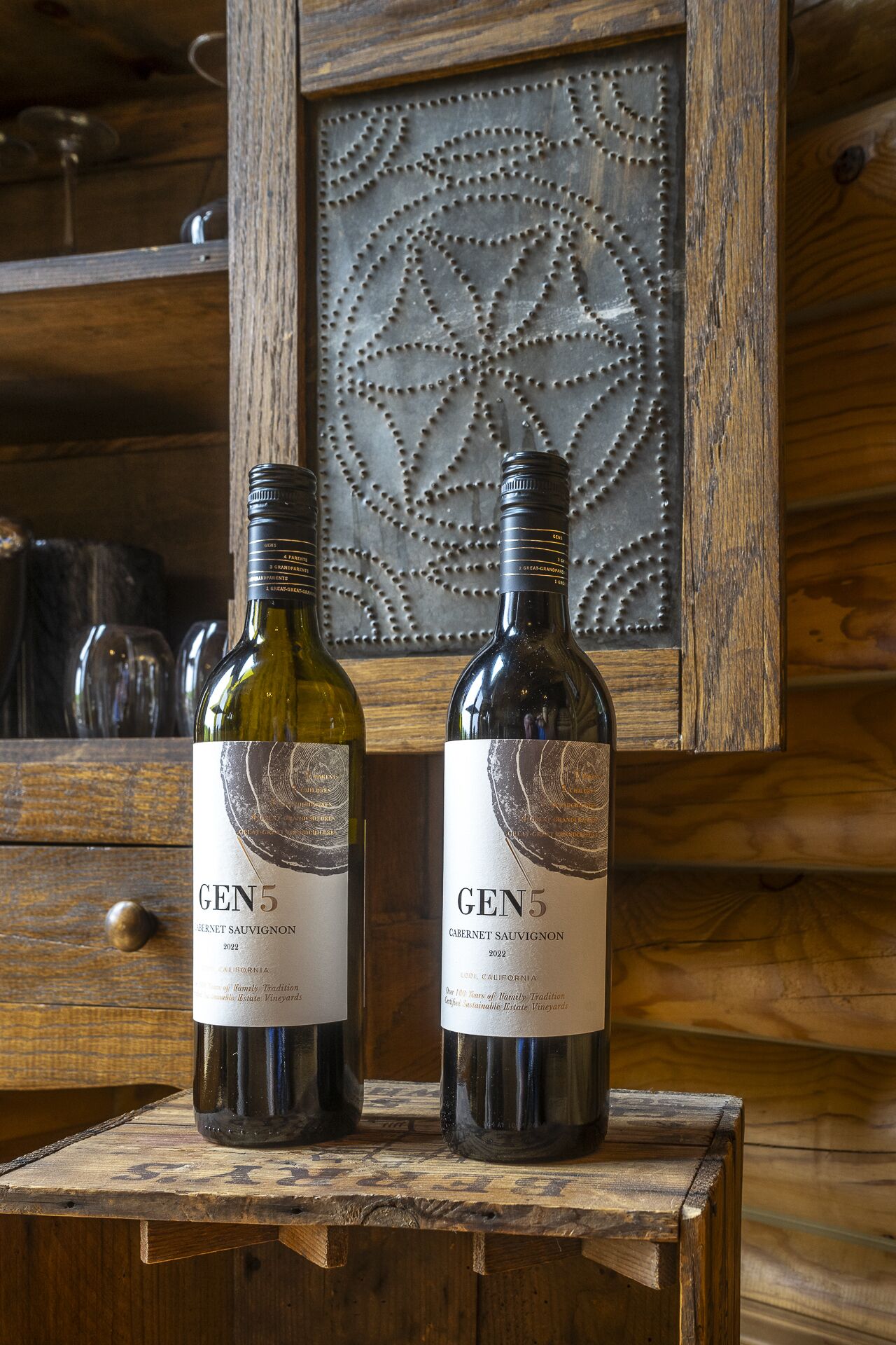 Duas garrafas de Cabernet Sauvignon 2022 GEN5 sobre uma mesa de madeira com um fundo rústico.
