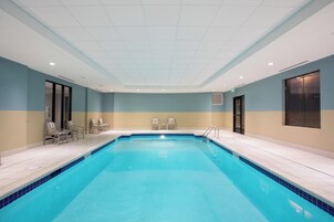 Piscina com borda azulejada, cercada por cadeiras de descanso e piso revestido de azulejos.