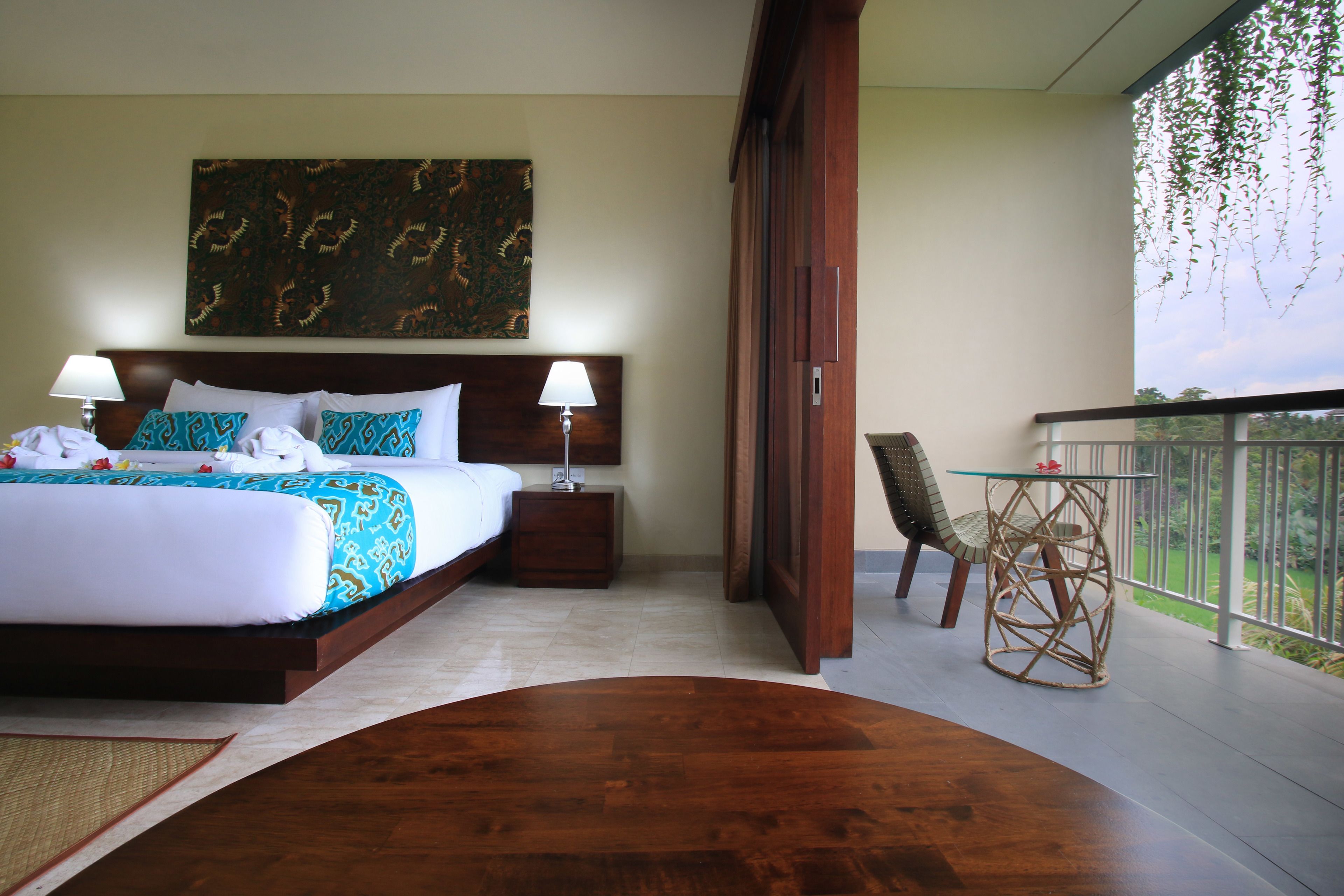 Quarto de hotel com cama, mesas de cabeceira, uma cadeira e varanda com vista.