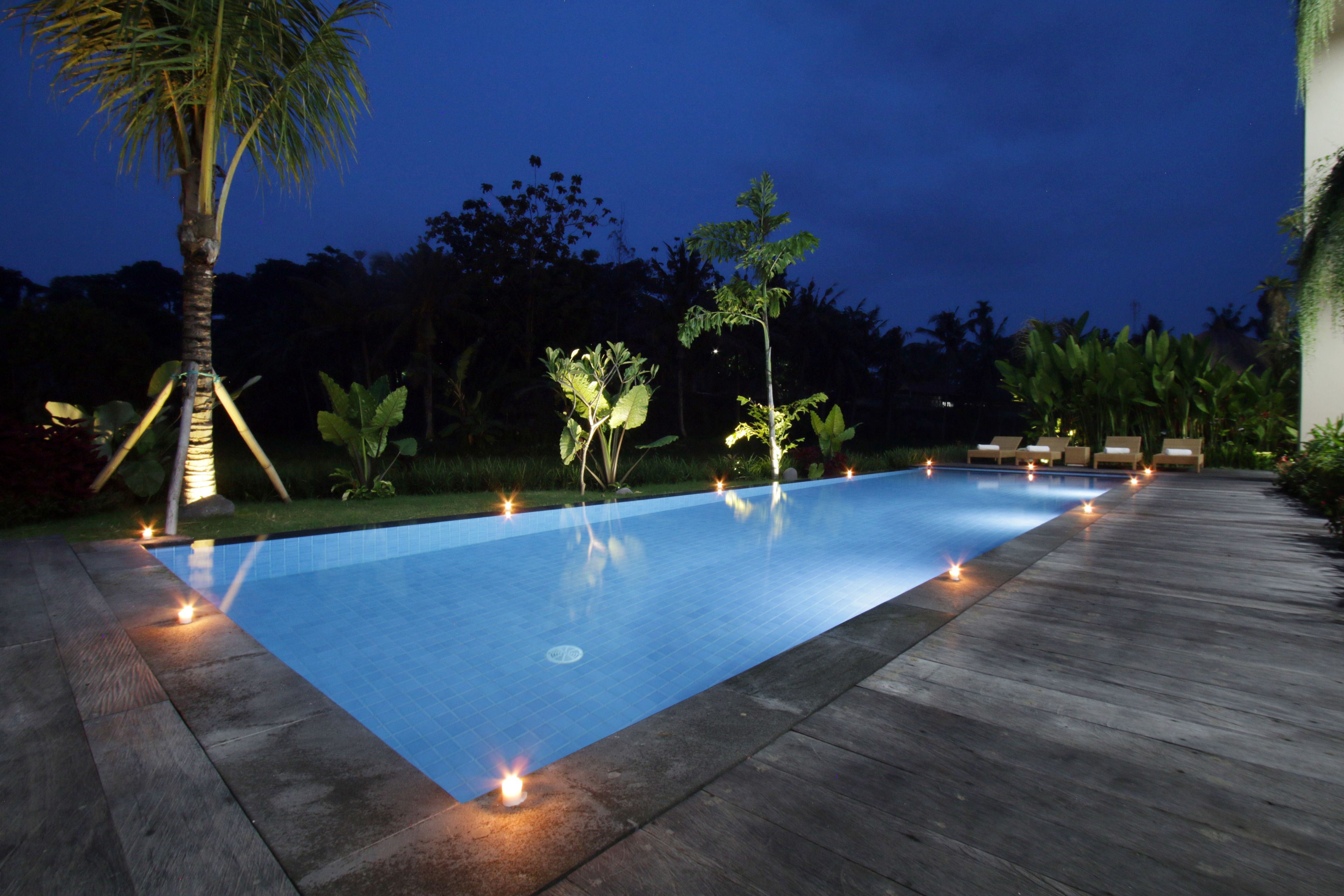 Uma piscina retangular com um deck de madeira ao redor, iluminada por pequenas luzes.