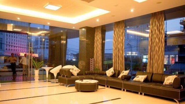 Um lobby moderno de hotel com uma grande área de estar, um balcão de recepção e amplas janelas com vista para a cidade.