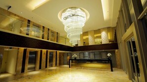 Um hall espaçoso com um lustre imponente, um balcão de recepção e um design moderno com grades de vidro e piso de mármore.