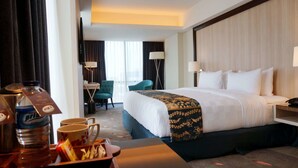 Quarto de hotel com uma cama grande, uma mesa de trabalho com cadeira, minibar e vista para a cidade.