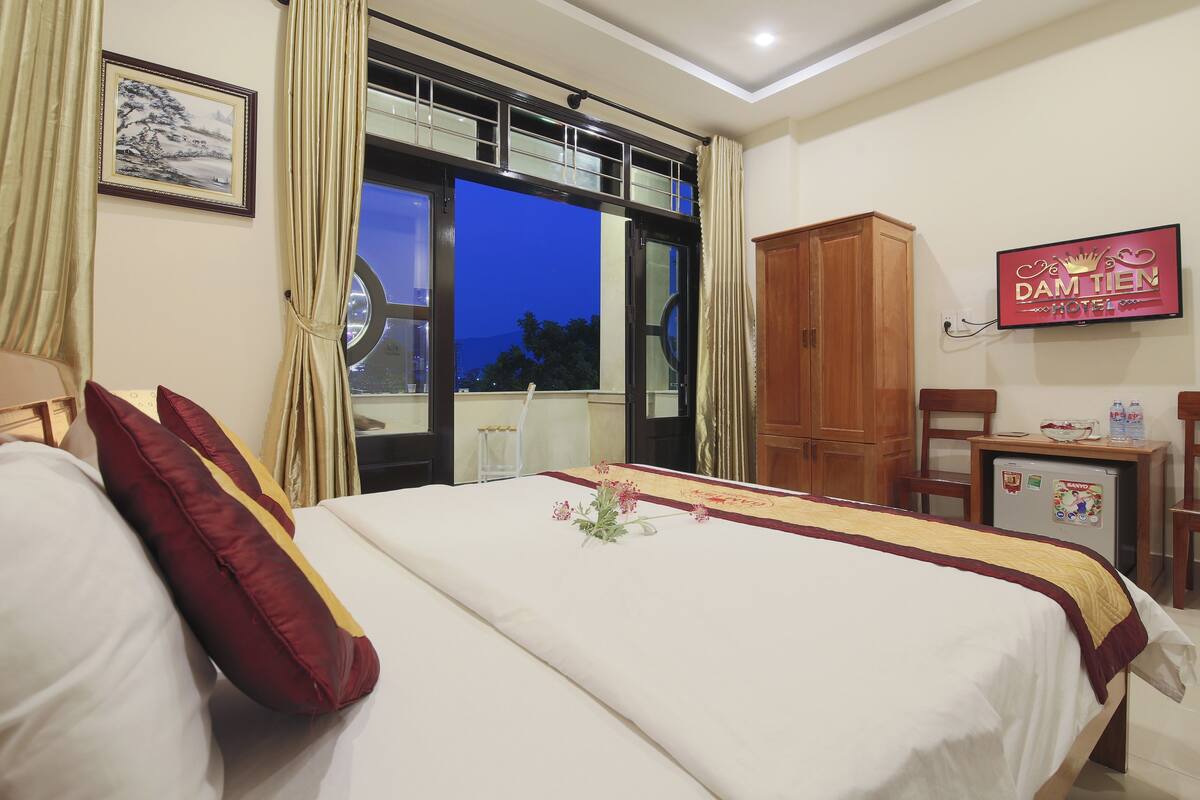 Quarto de hotel com uma cama grande, uma escrivaninha, um guarda-roupa e uma televisão exibindo o nome do hotel.