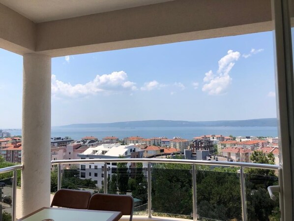Varanda com mesa e cadeiras, vista para um horizonte costeiro com edifícios e céu claro.