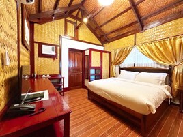 Quarto de hotel com teto de madeira, uma cama, uma secretária com telefone e janela com cortinas.