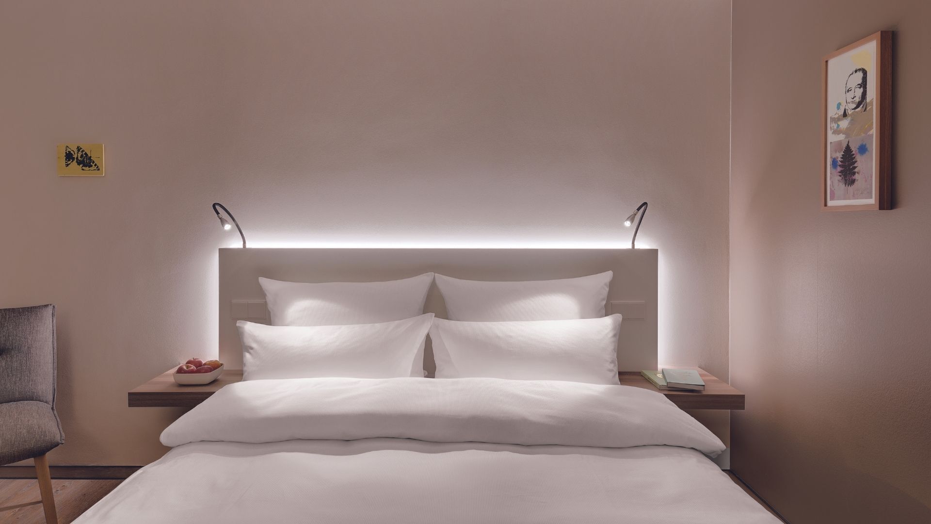 Quarto moderno com uma cama grande, mesas de cabeceira, uma cadeira e uma obra de arte na parede.