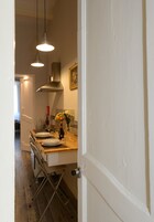 Uma cozinha estreita com bancada de madeira, duas luminárias pendentes e uma porta branca.