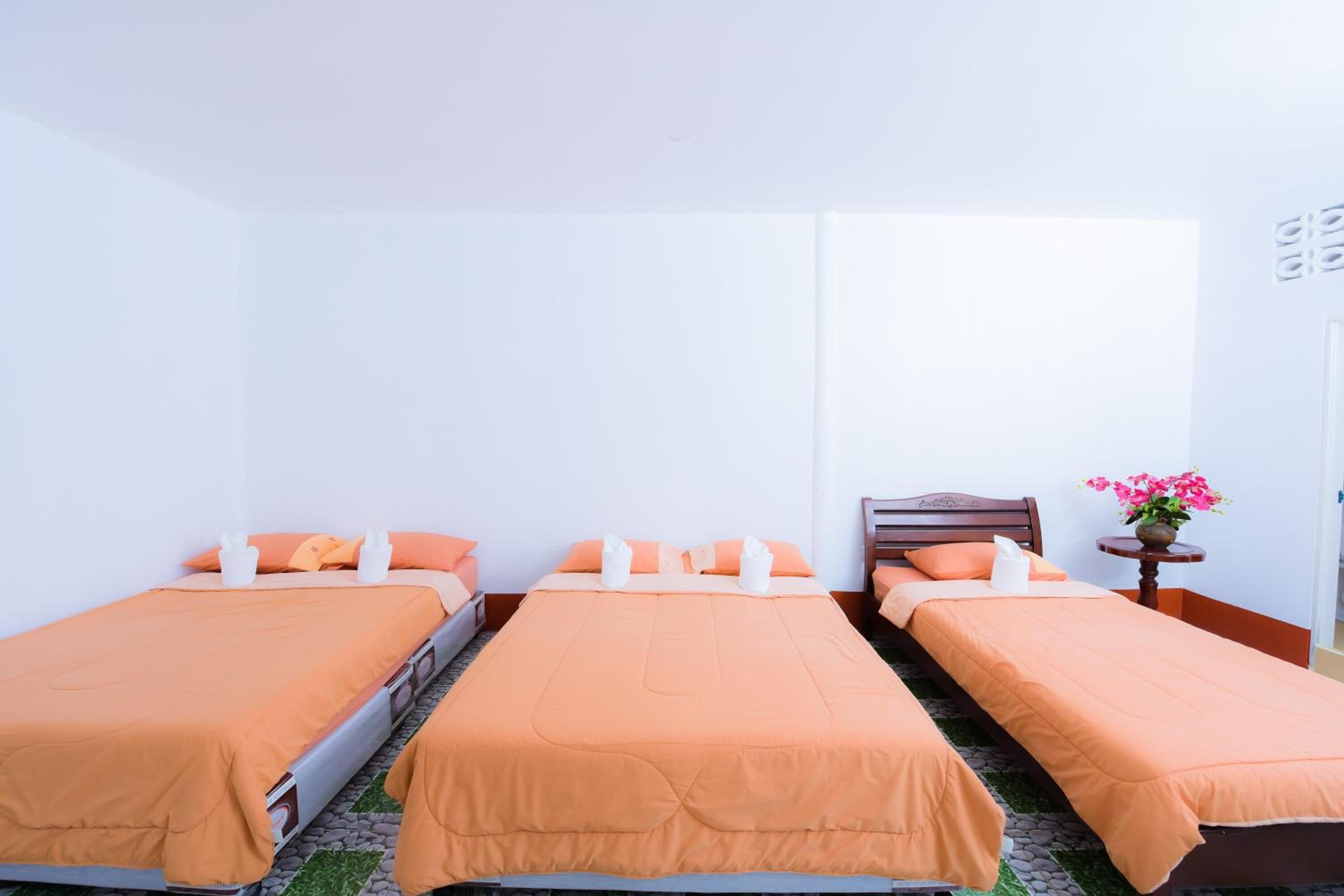 Quarto de hotel com duas camas de solteiro, cada uma com colcha laranja e almofadas brancas. Há uma pequena mesa com um vaso de flores à direita das camas.