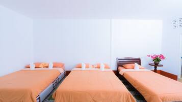 Quarto de hotel com duas camas de solteiro, cada uma com colcha laranja e almofadas brancas. Há uma pequena mesa com um vaso de flores à direita das camas.