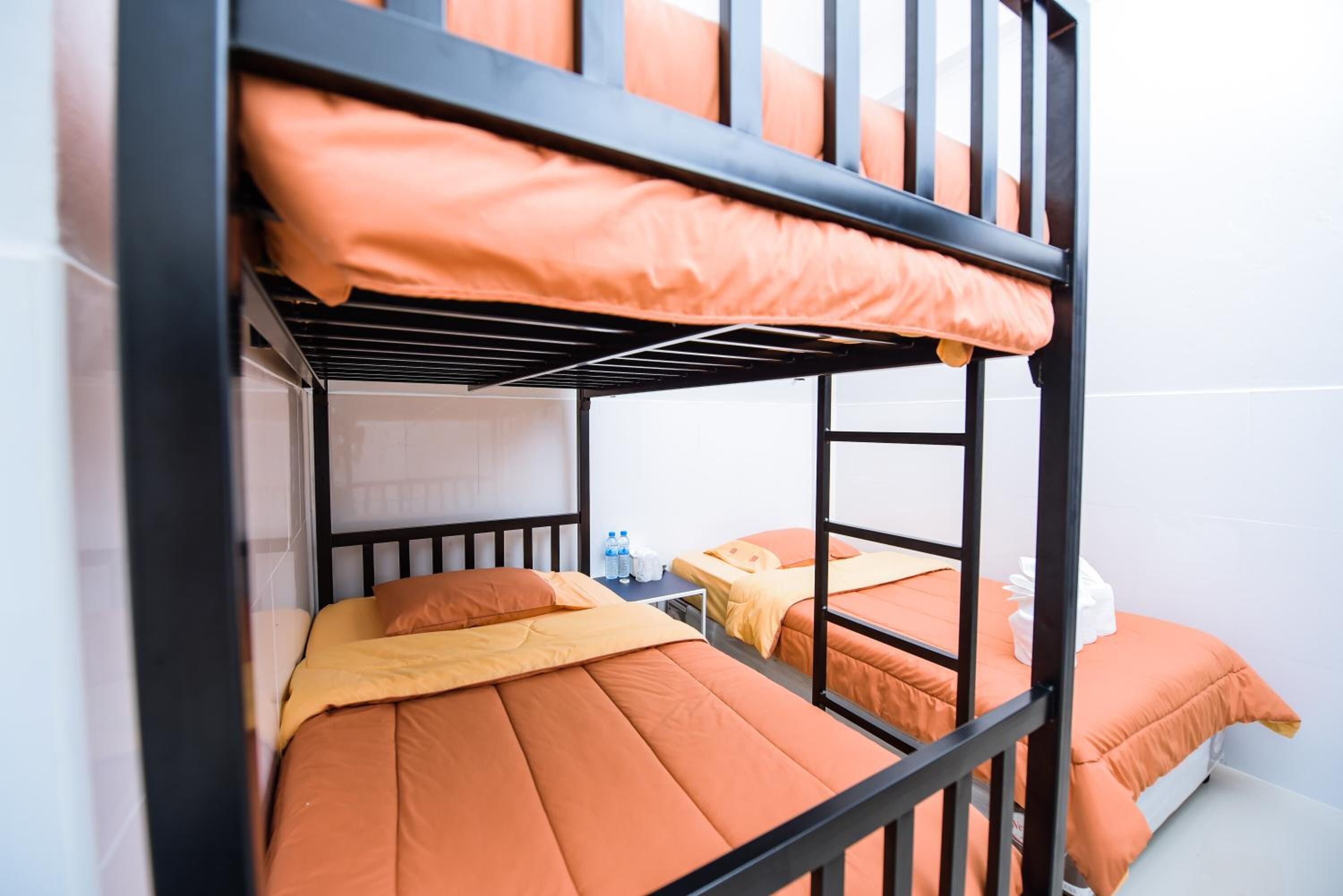 Quarto com beliches, roupa de cama laranja e estrutura de metal preta.