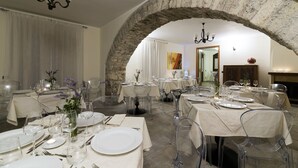 Uma sala de jantar com mesas postas para refeição, cadeiras vazias e um arco de pedra.