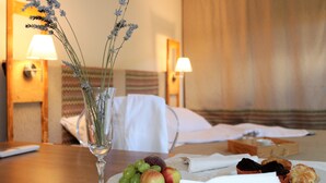 Quarto de hotel com uma mesa de jantar posta com frutas, doces e um vaso de flores.