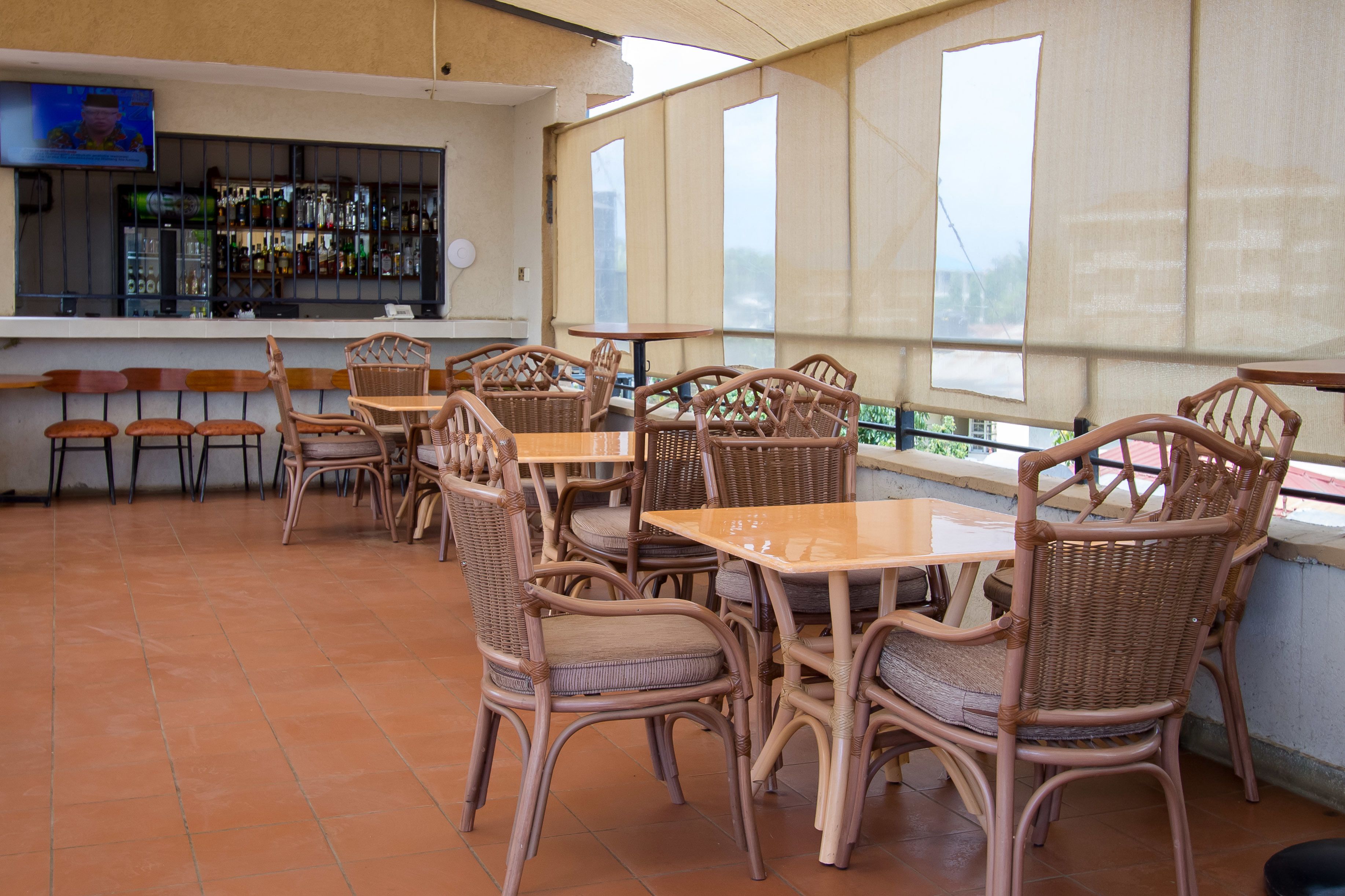 Restaurante com mobiliário de vime, área de bar e grandes janelas.