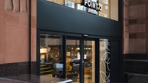Entrada de hotel com design moderno, incluindo fachada de vidro e uma placa com a inscrição "POINT HOTEL".