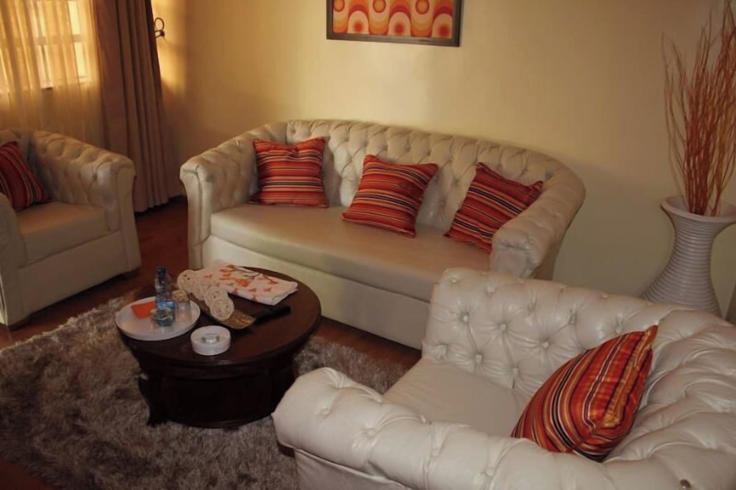 Uma sala de estar com um sofá branco, uma mesa de centro e um vaso com plantas secas.
