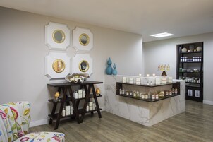 Interior moderno com uma receção em mármore, estantes com velas e produtos de higiene, e uma parede decorativa com espelhos.