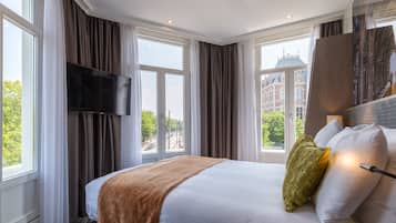 Quarto de hotel com uma cama grande, televisão de tela plana na parede e vista da cidade por amplas janelas.