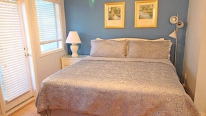 Um quarto com uma cama, uma mesa de cabeceira, uma luminária e duas molduras na parede.