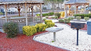 Um gazebo com cerca de madeira, rodeado por jardins ajardinados e cobertura de palha.