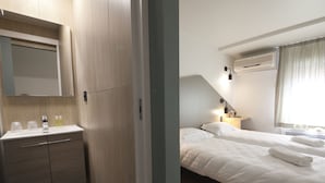 Quarto de hotel com guarda-roupa de madeira, mesa de cabeceira com abajur e cama com roupa de cama e toalhas brancas.