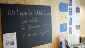 Quadro negro com mensagem de boas-vindas em francês, link para uma página do Facebook e diversos cartazes informativos numa parede de madeira.