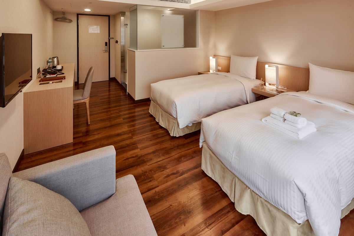Quarto de hotel com duas camas, uma escrivaninha, uma cadeira e uma televisão.